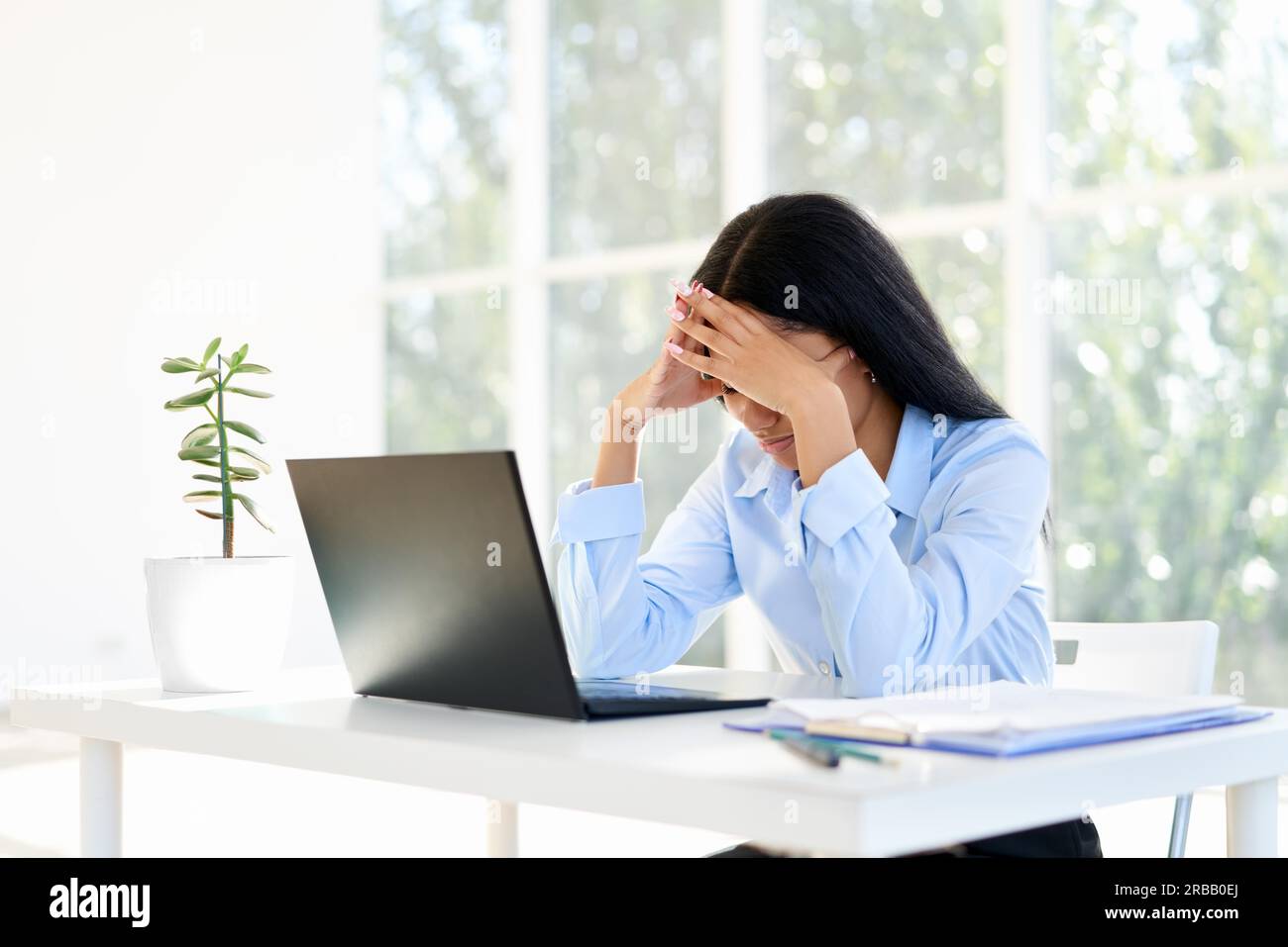 Stressed tired businesswoman closed face by two hands sitting in modern ...