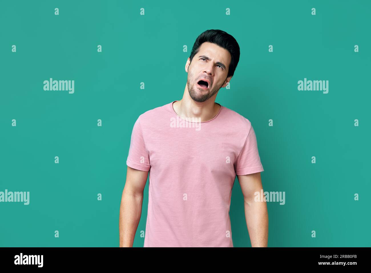 Funny displeased man in pink t- shirt looking up on blue background ...