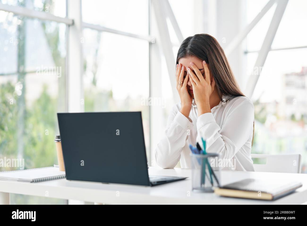 Stressed tired businesswoman closed face by two hands sitting in modern ...