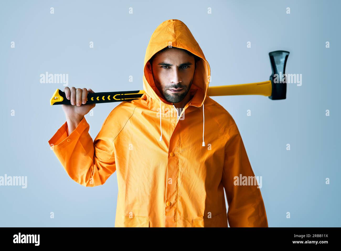 Young serious man in bright raincoat holding big ax on his shoulder ...