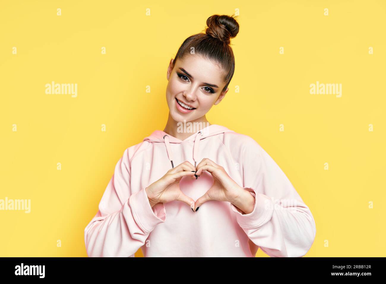Young smiling pretty woman making heart symbol by hands on yellow ...