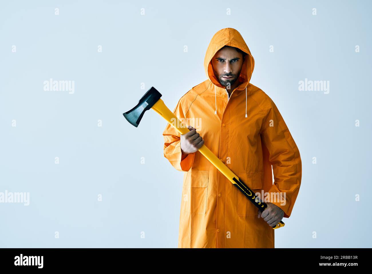 Young serious man in bright raincoat holding big axe in hands with copy ...