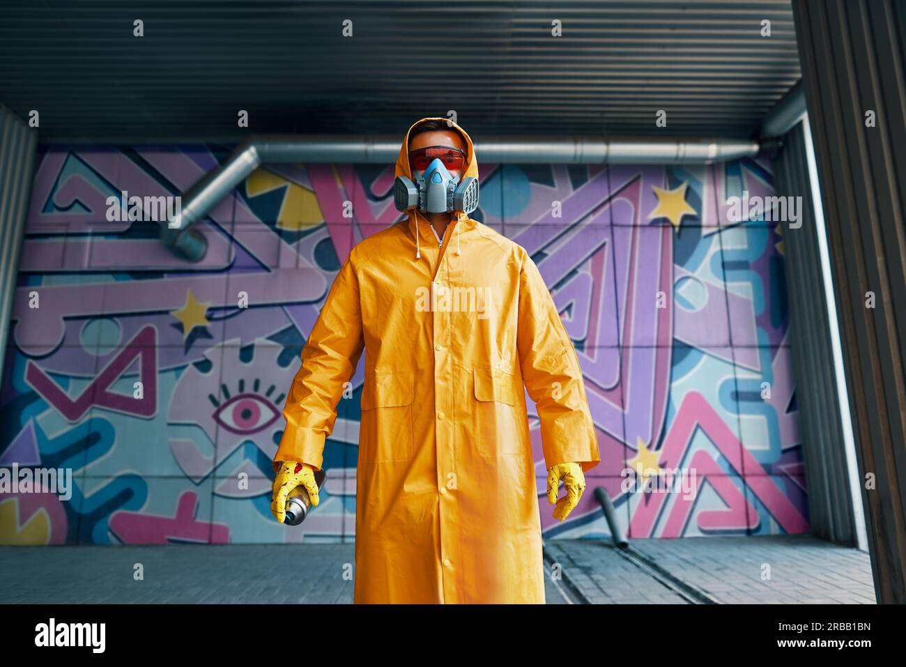 Graffiti painter in respirator mask standing near the wall with his ...