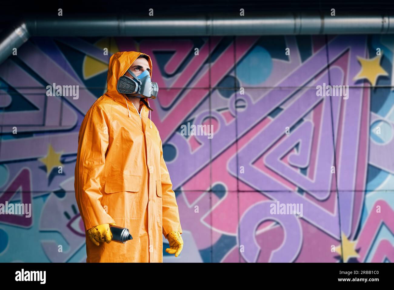 Graffiti painter in respirator mask standing near the wall with his ...