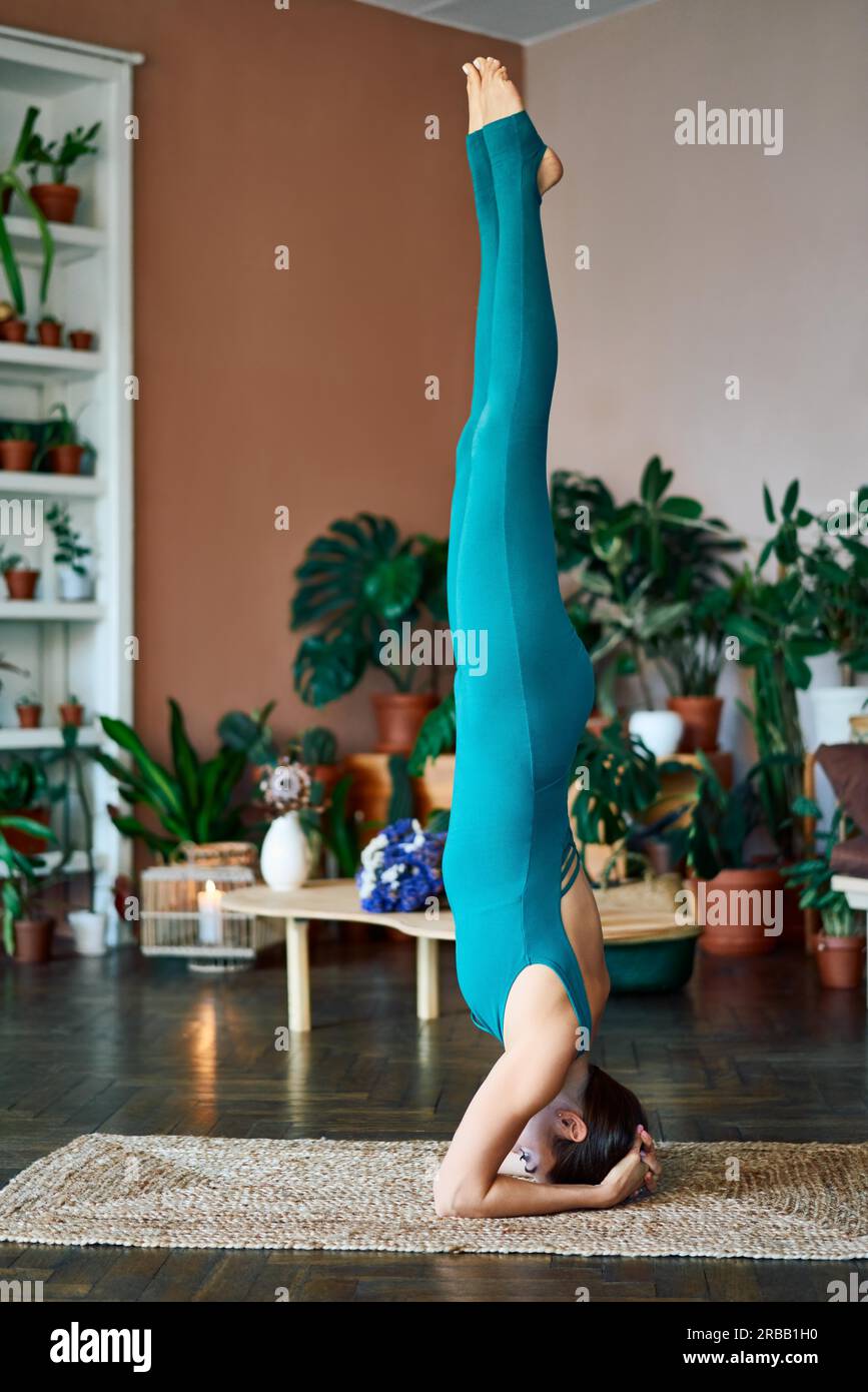 Young slim woman doing yoga asana supported headstand at home. Salamba ...