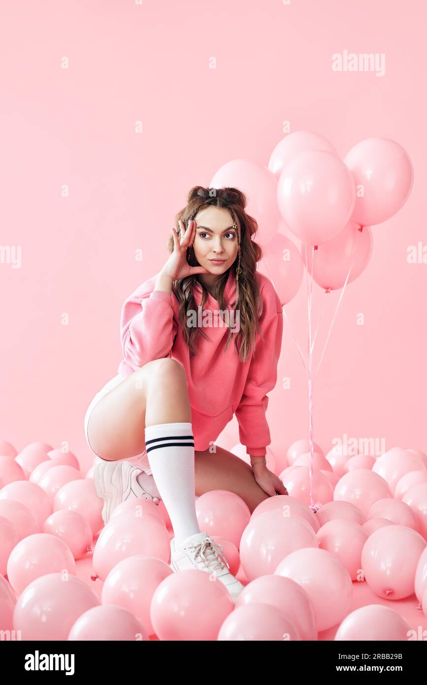 Bored fashionable woman sitting on floor with pink air balloons on pink ...