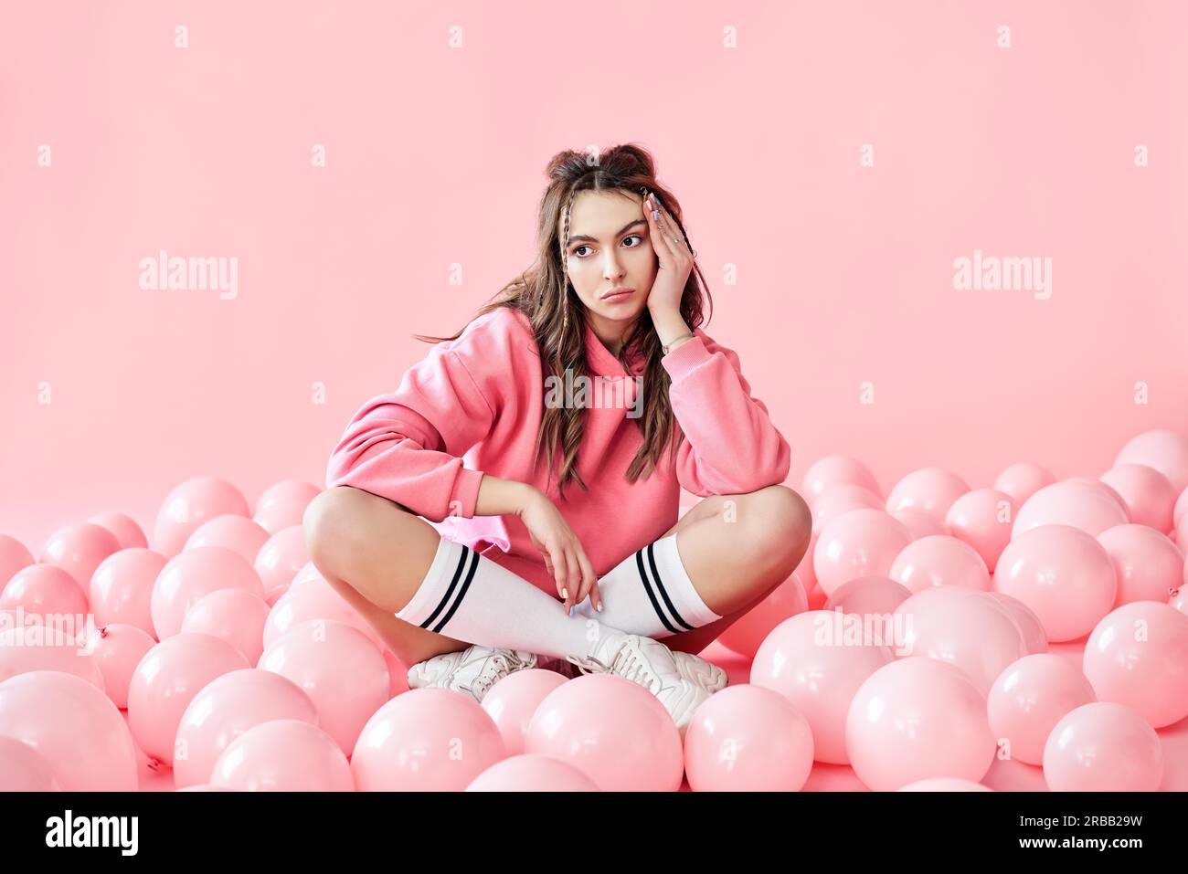 Bored fashionable woman sitting on floor with pink air balloons on pink ...