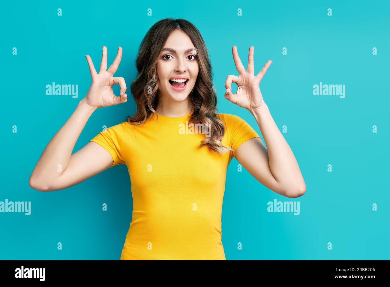 Pretty smiling woman showing OK sign with fingers over blue background ...