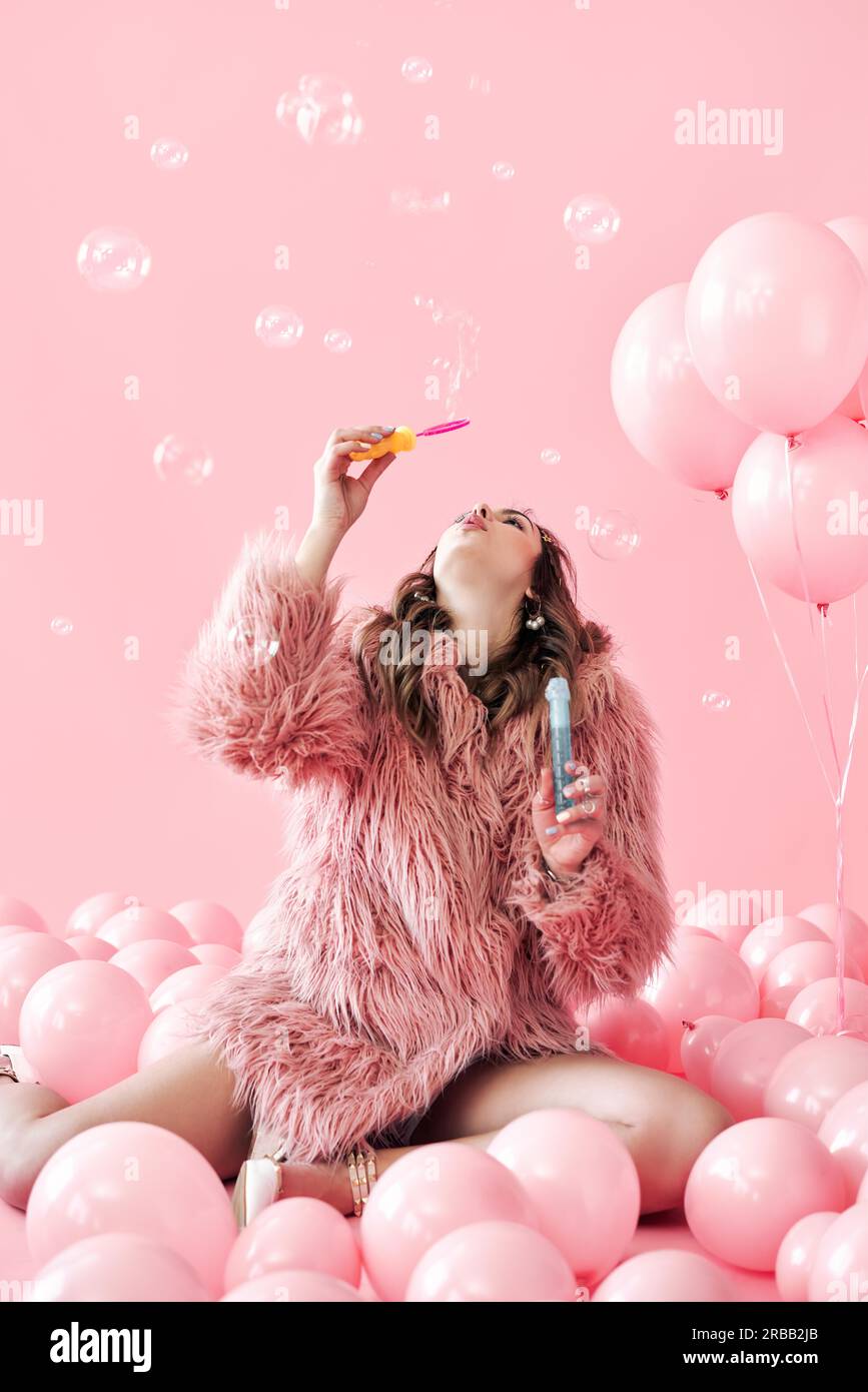 Young pretty woman blowing soap bubbles on pink background with ...