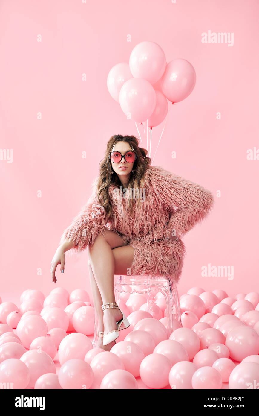 Confident fashion woman sitting on chair posing on many pink balloons ...