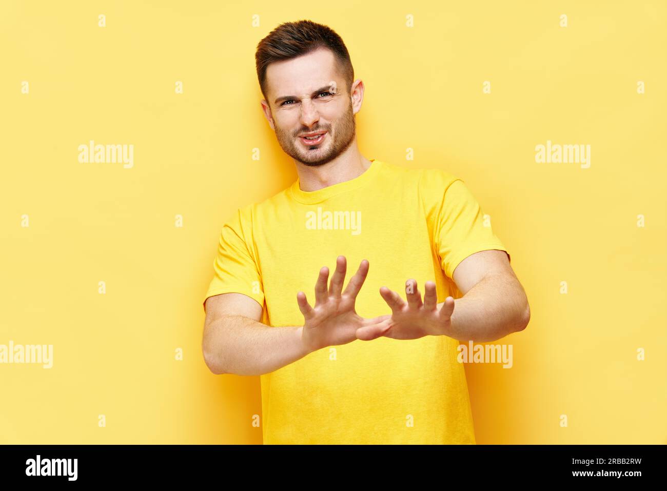 Young displeased man making stop gesture sign say no isolated on yellow ...