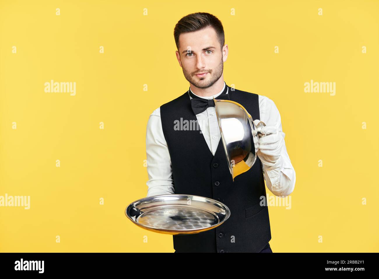 Elegant young waiter holding cloche over empty tray ready to serve on ...