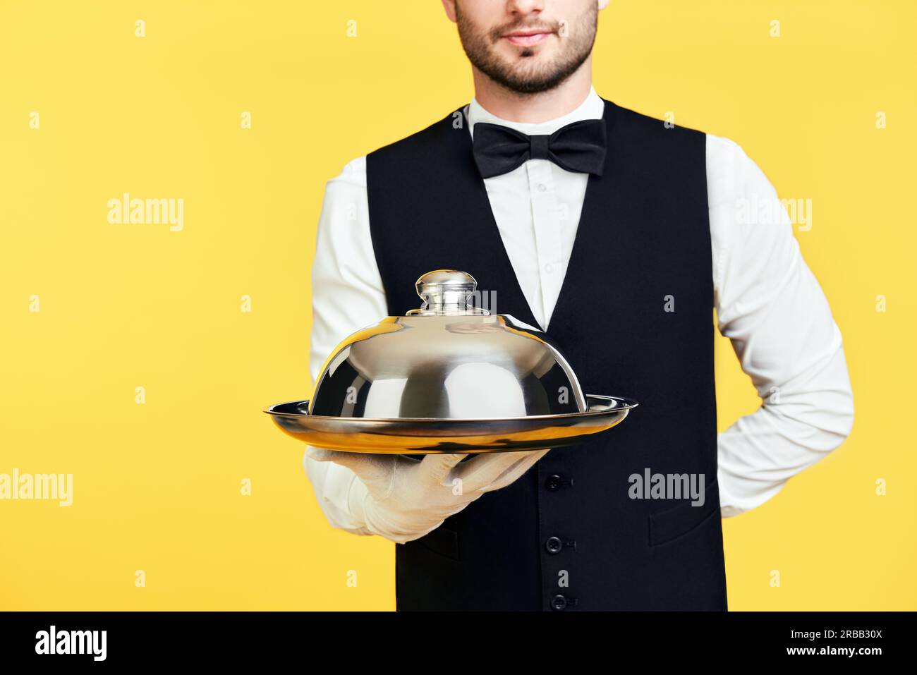 Young handsome waiter holding metal tray with cover ready to serve on ...