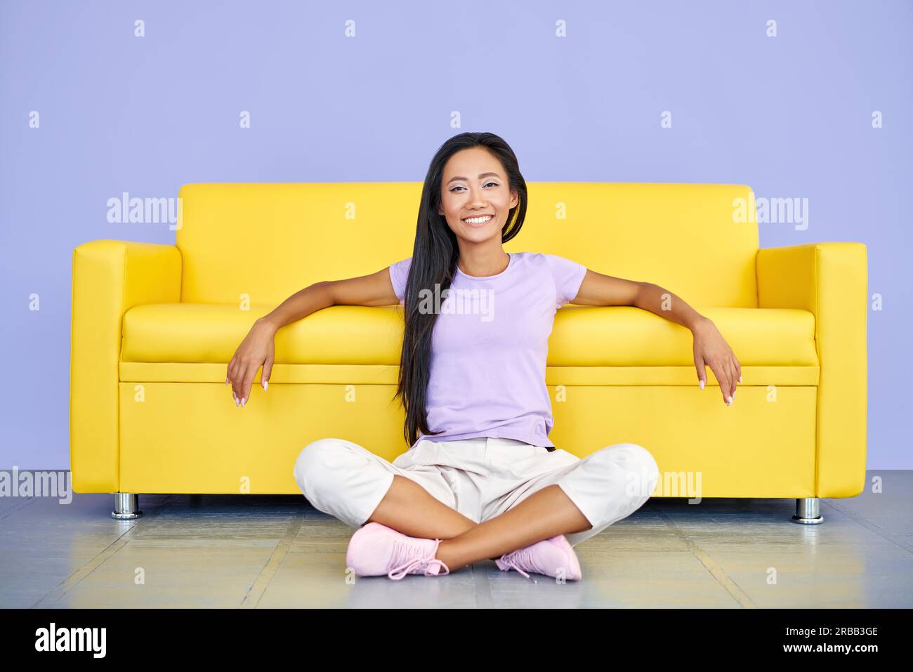 Happy smiling asian woman relax sitting on floor leaning yellow sofa ...