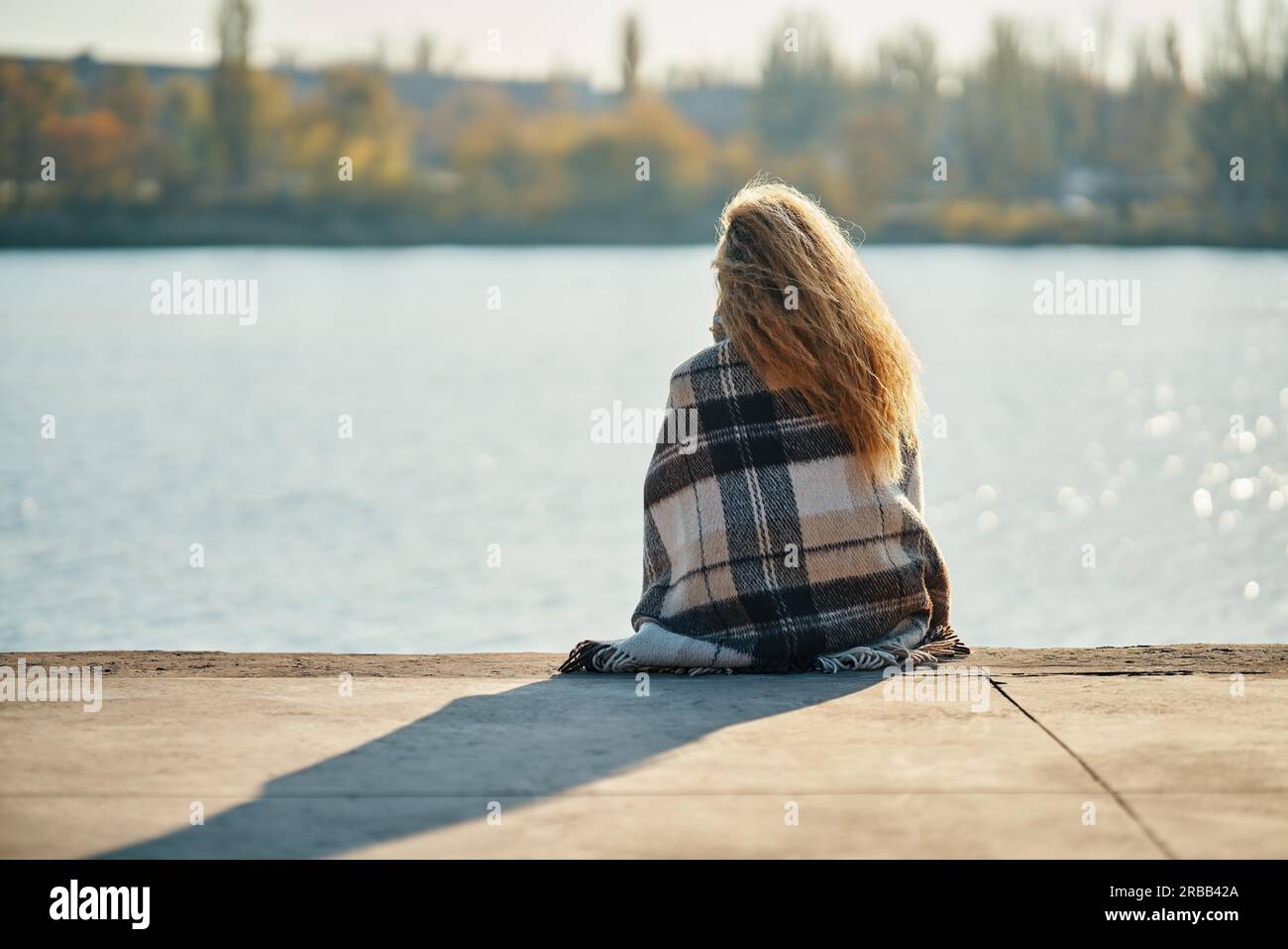 Back view of young woman relaxing alone by a river in the city wrapped ...