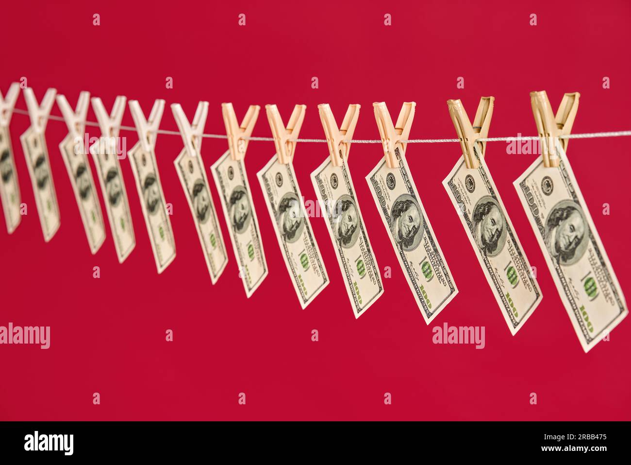 Money laundering, US dollars hanging on rope over red studio background ...