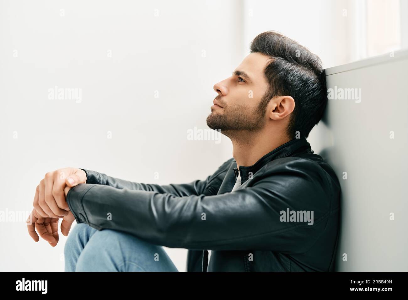 Portrait of handsome thoughtful man sitting on floor leaning to the ...