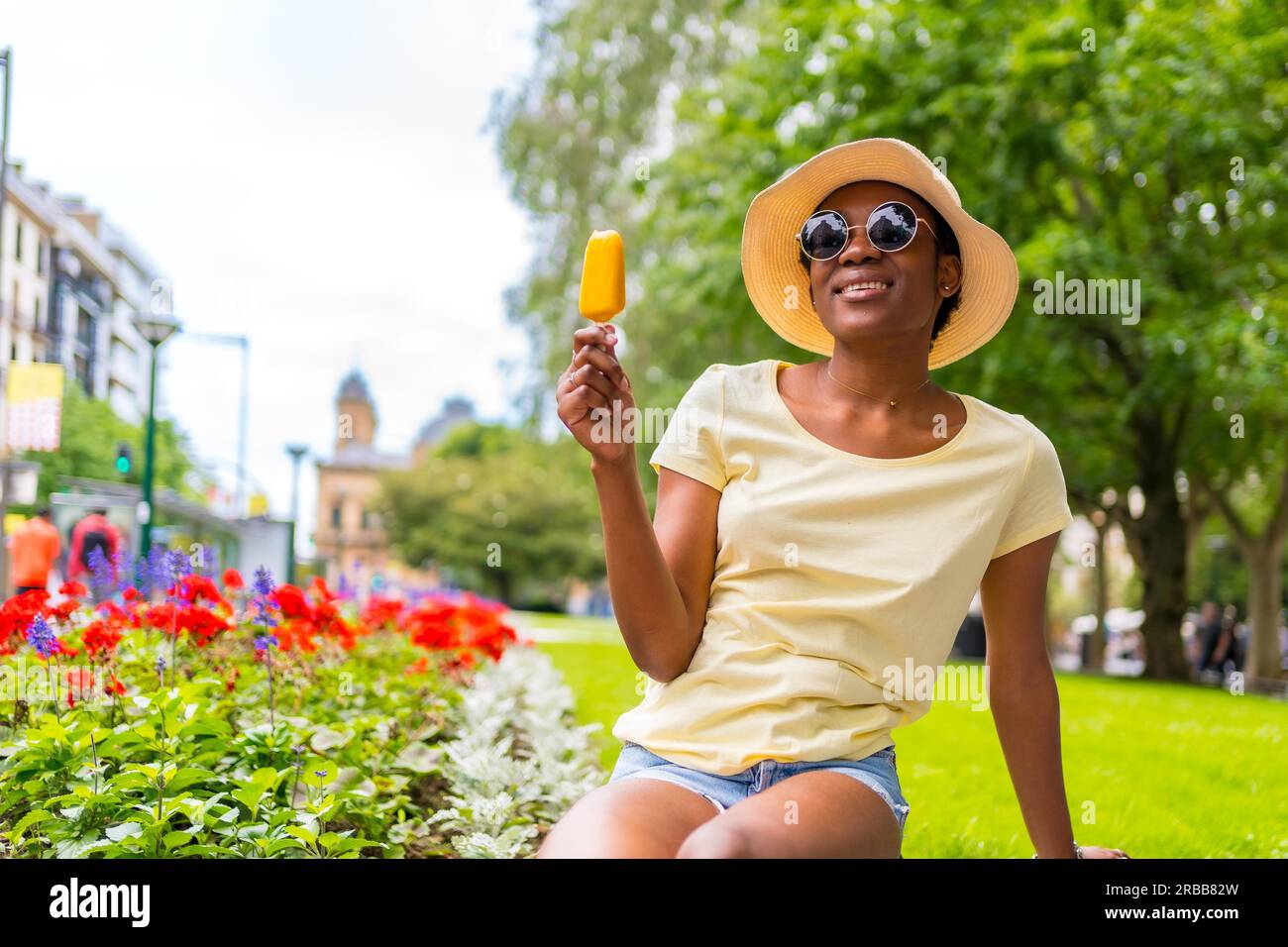 African black ethnicity woman eating a mango ice cream in the city ...