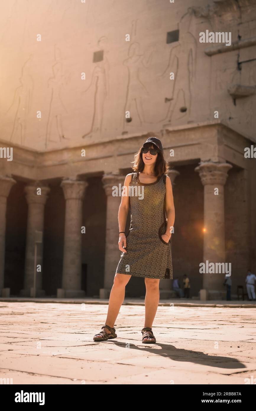 A young tourist wearing a cap visiting the Edfu Temple at sunrise in ...