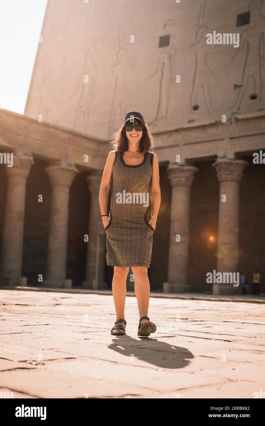 A young tourist wearing a cap visiting the Edfu Temple at sunrise in ...