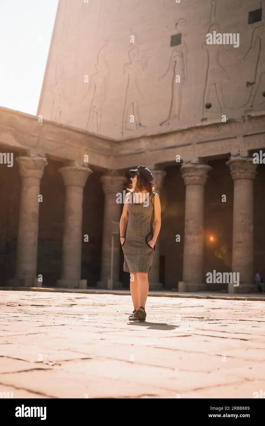 A young tourist wearing a cap visiting the Edfu Temple at sunrise in ...