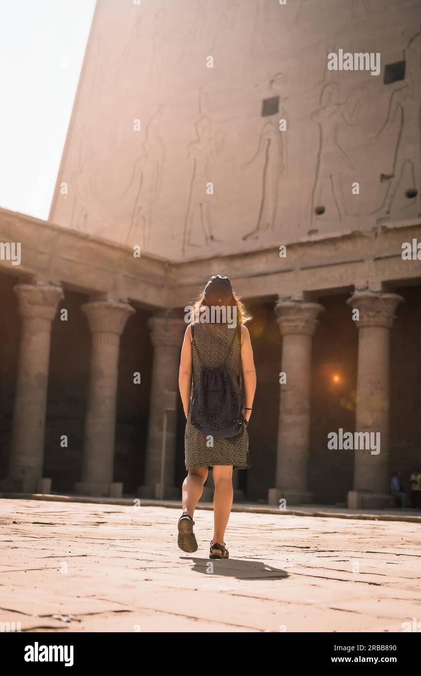 A young tourist wearing a cap visiting the Edfu Temple at sunrise in ...