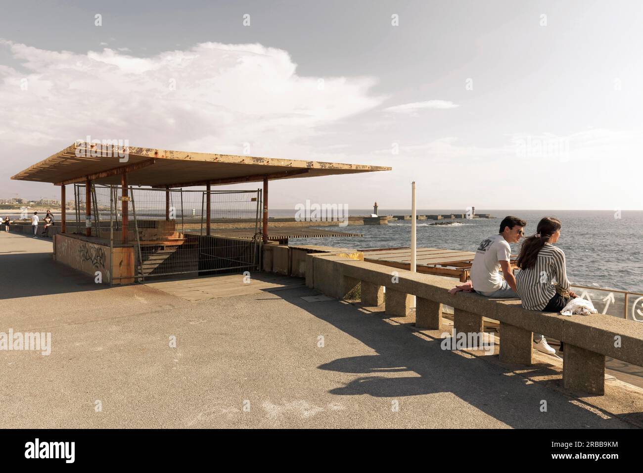 Waterfront Praia do Caneiro overlooking Atlantic Ocean, young couple sitting on a parapet ...