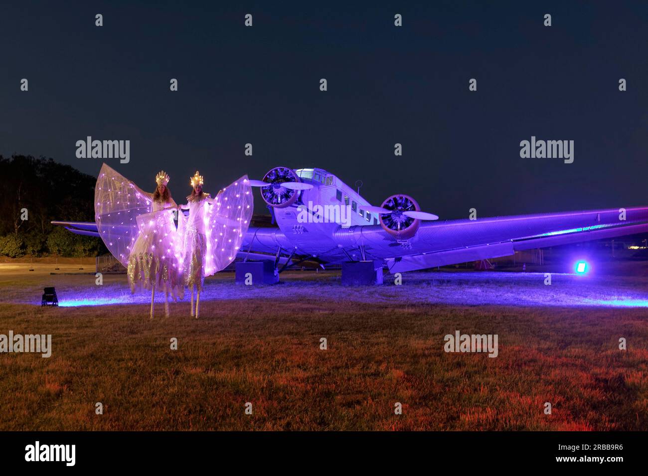 Illuminated winged creatures on stilts, walking act in front of the ...
