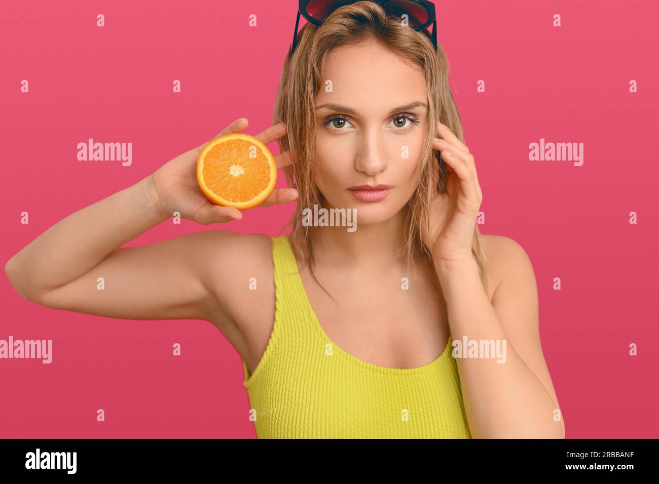 Pretty Young Blond Woman With Sunglasses On Top Of Her Head Holding A Fresh Halved Orange To Her