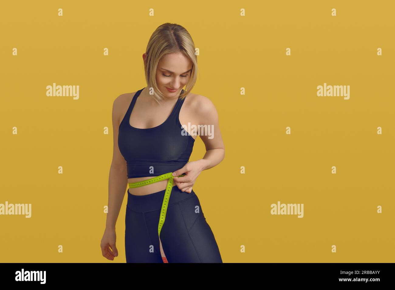 Slim sporty young woman measuring her waist with a tape measure as she ...