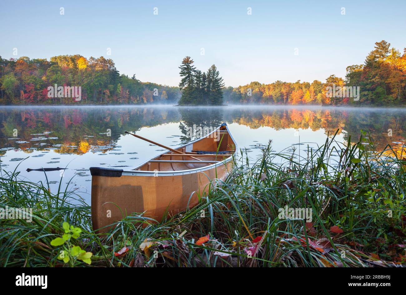Yellow canoe on shore of calm lake with island and trees in fall color ...