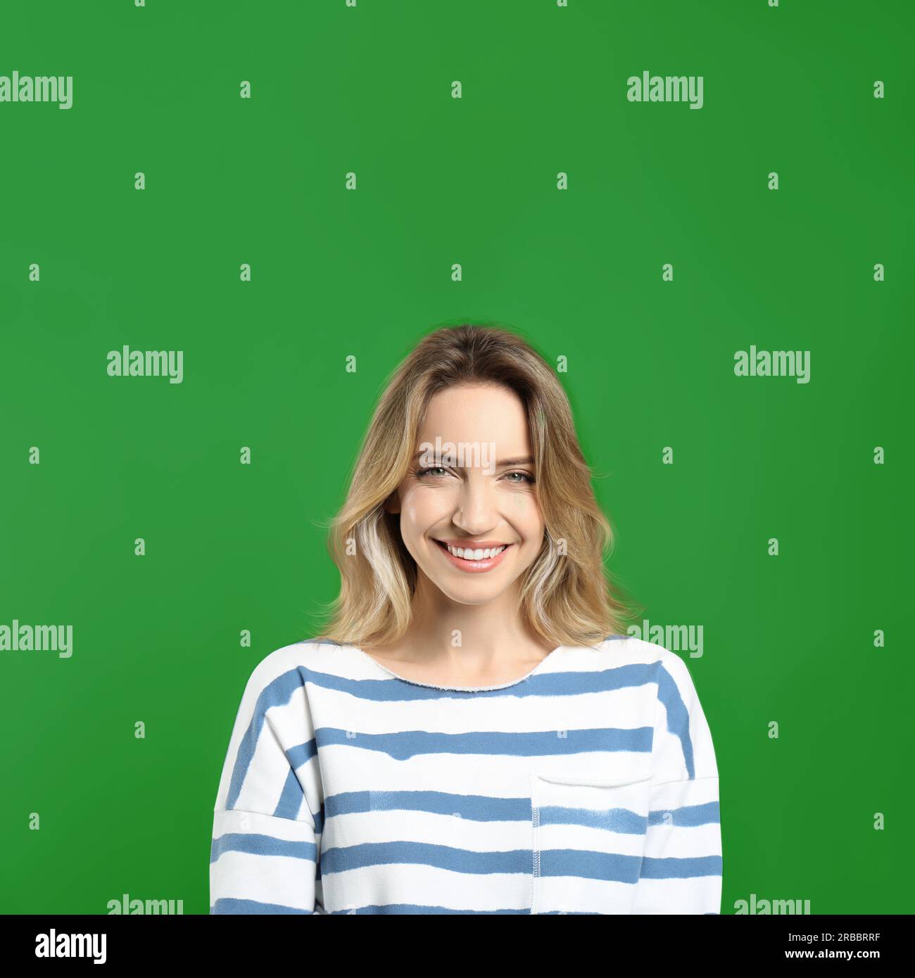 Chroma key compositing. Happy young woman smiling against green screen ...