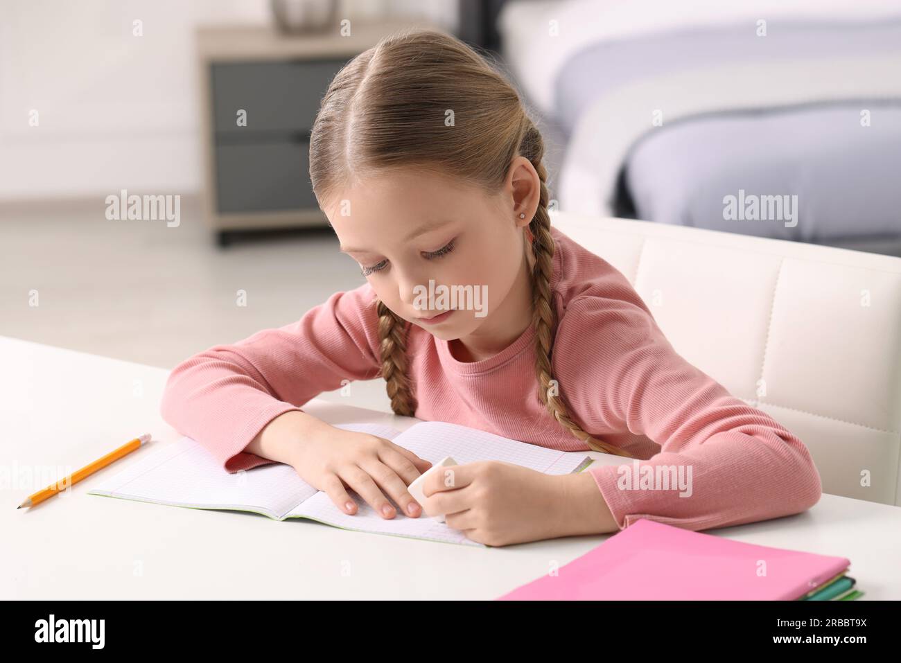 Girl using eraser at white desk in room Stock Photo - Alamy
