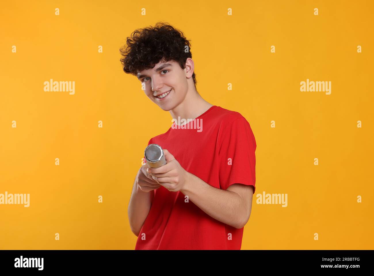 Portrait of happy teenage boy with party popper on orange background ...