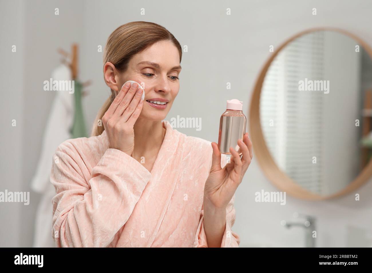 Beautiful woman removing makeup with cotton pad indoors, space for text ...