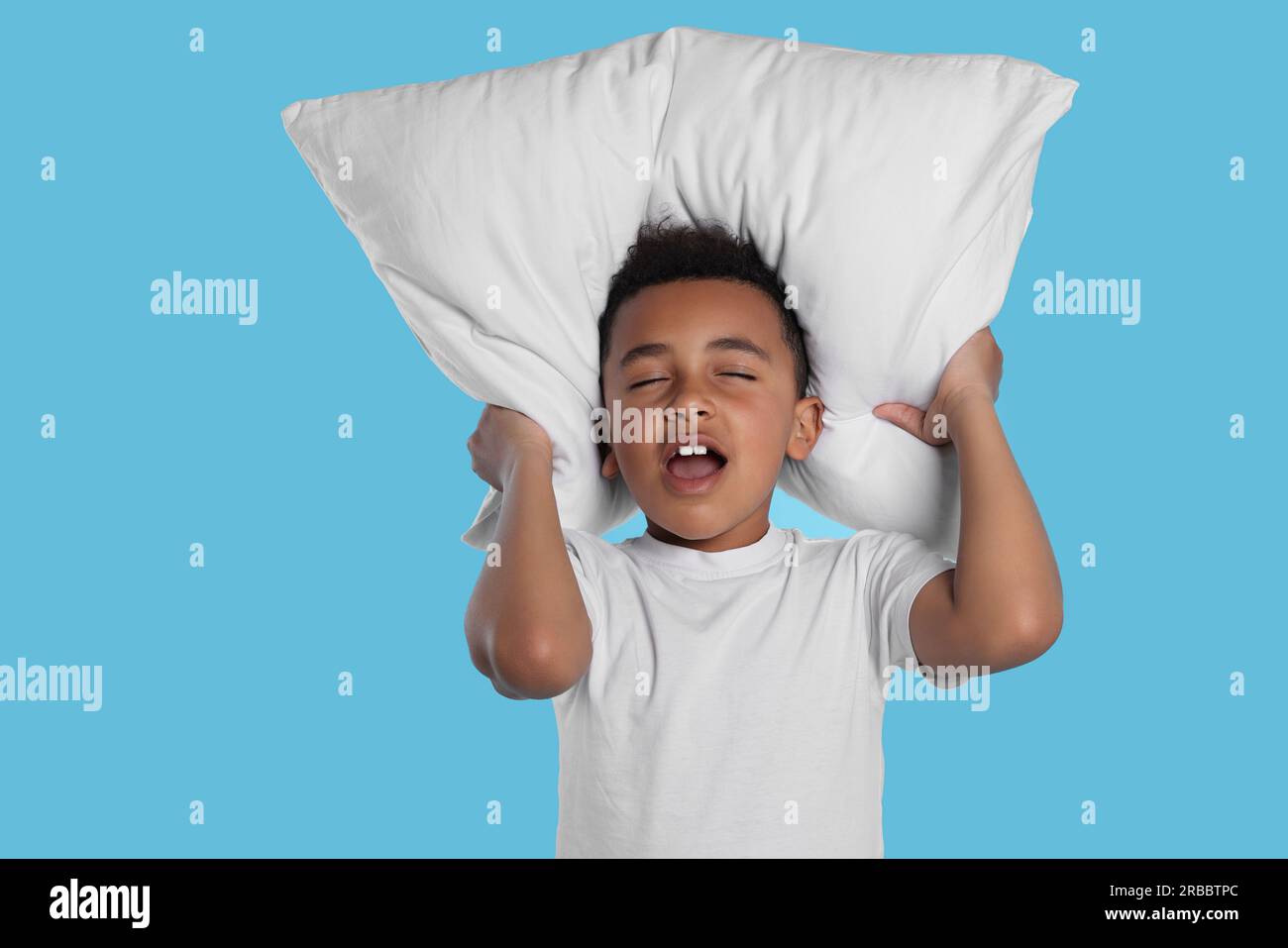 Boy covering his ears with pillow on light blue background. Insomnia ...