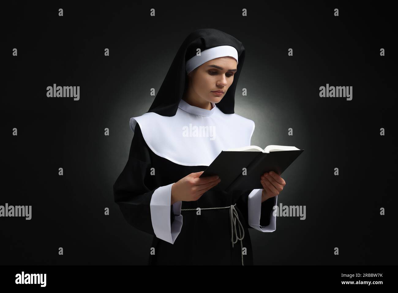 Young nun reading Bible on black background Stock Photo - Alamy