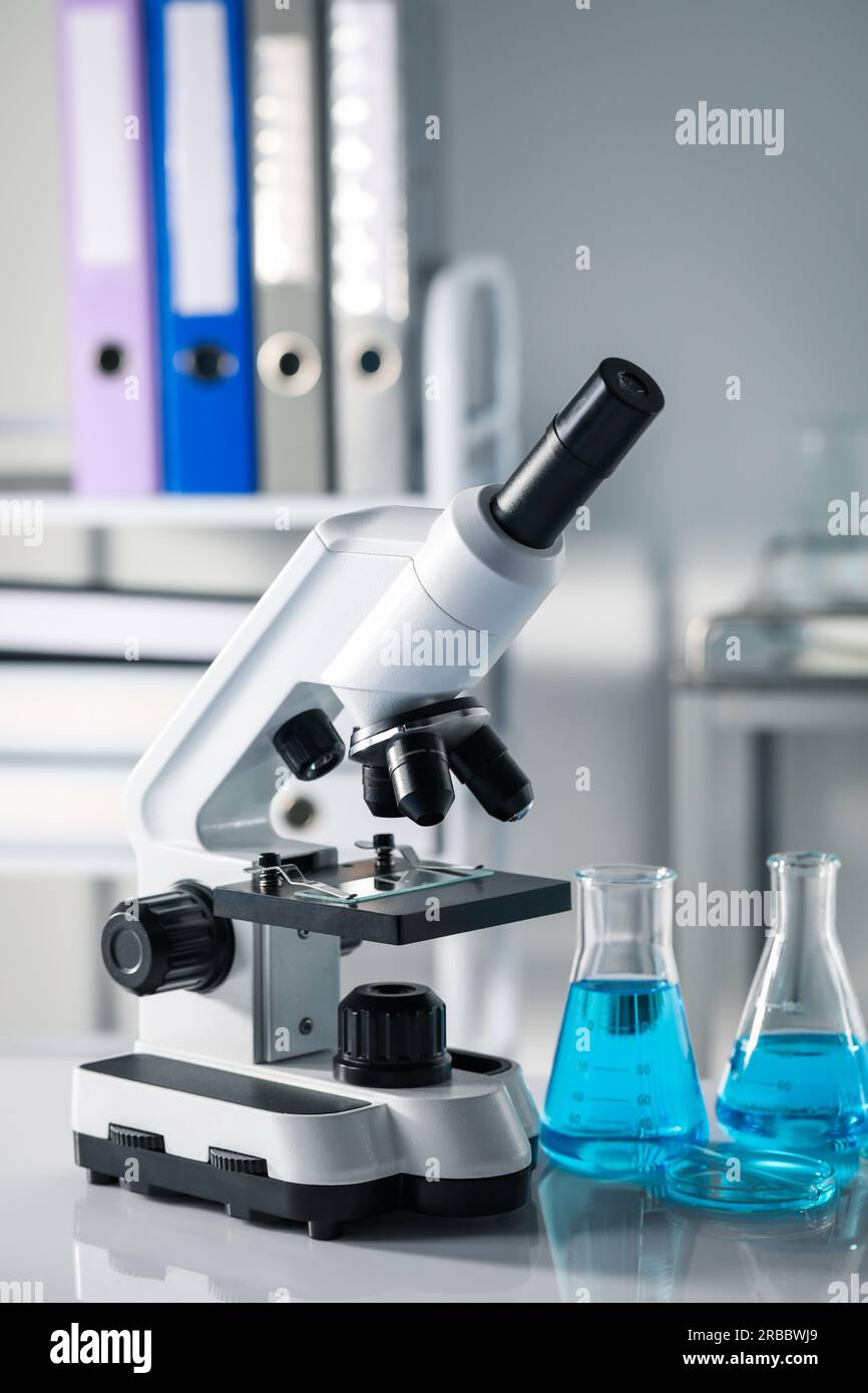 Different laboratory glassware with light blue liquid and microscope on ...