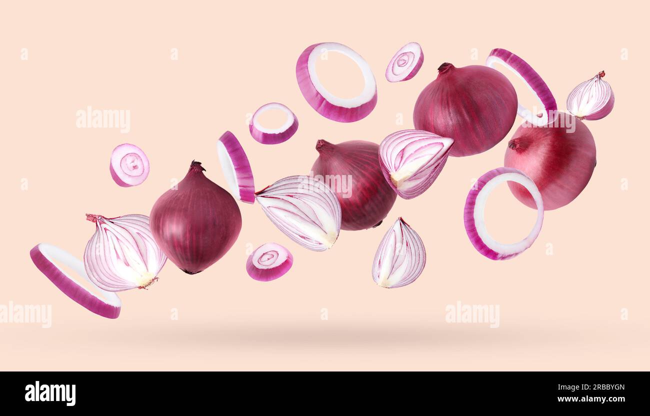 Whole and cut fresh red onions falling on light coral background Stock ...