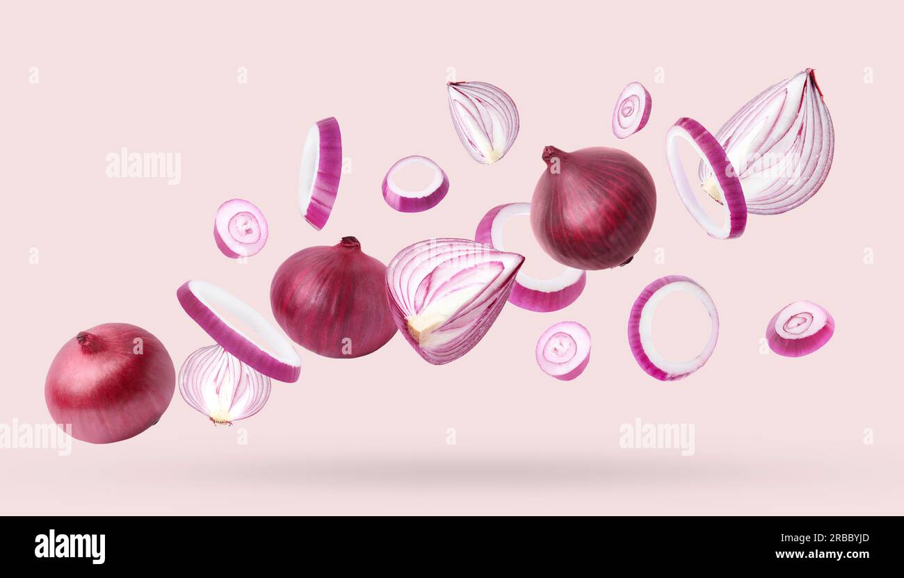 Whole and cut fresh red onions falling on light pink background Stock ...