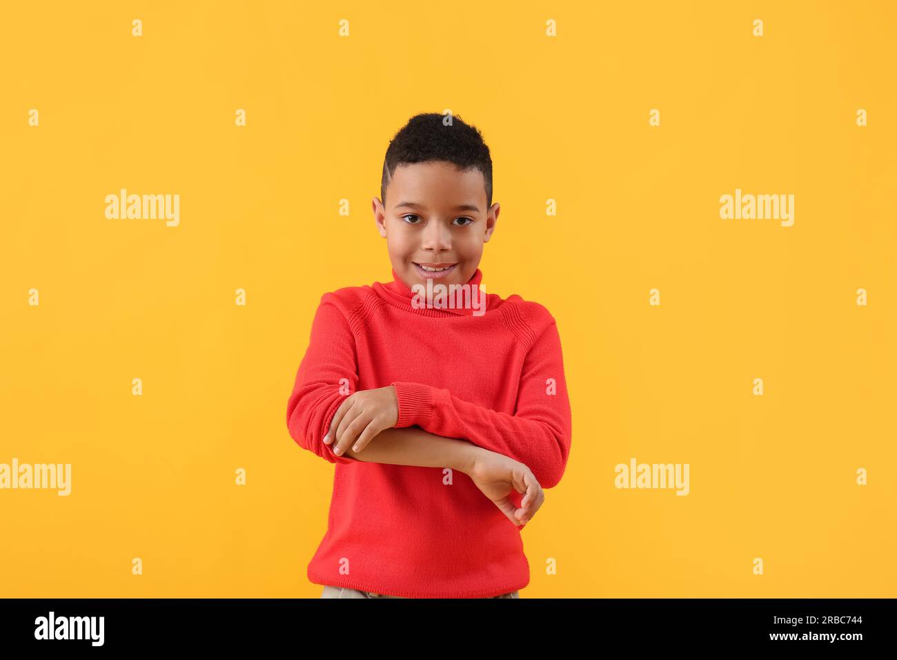 Little African-American boy rolling up his sleeve on yellow background ...