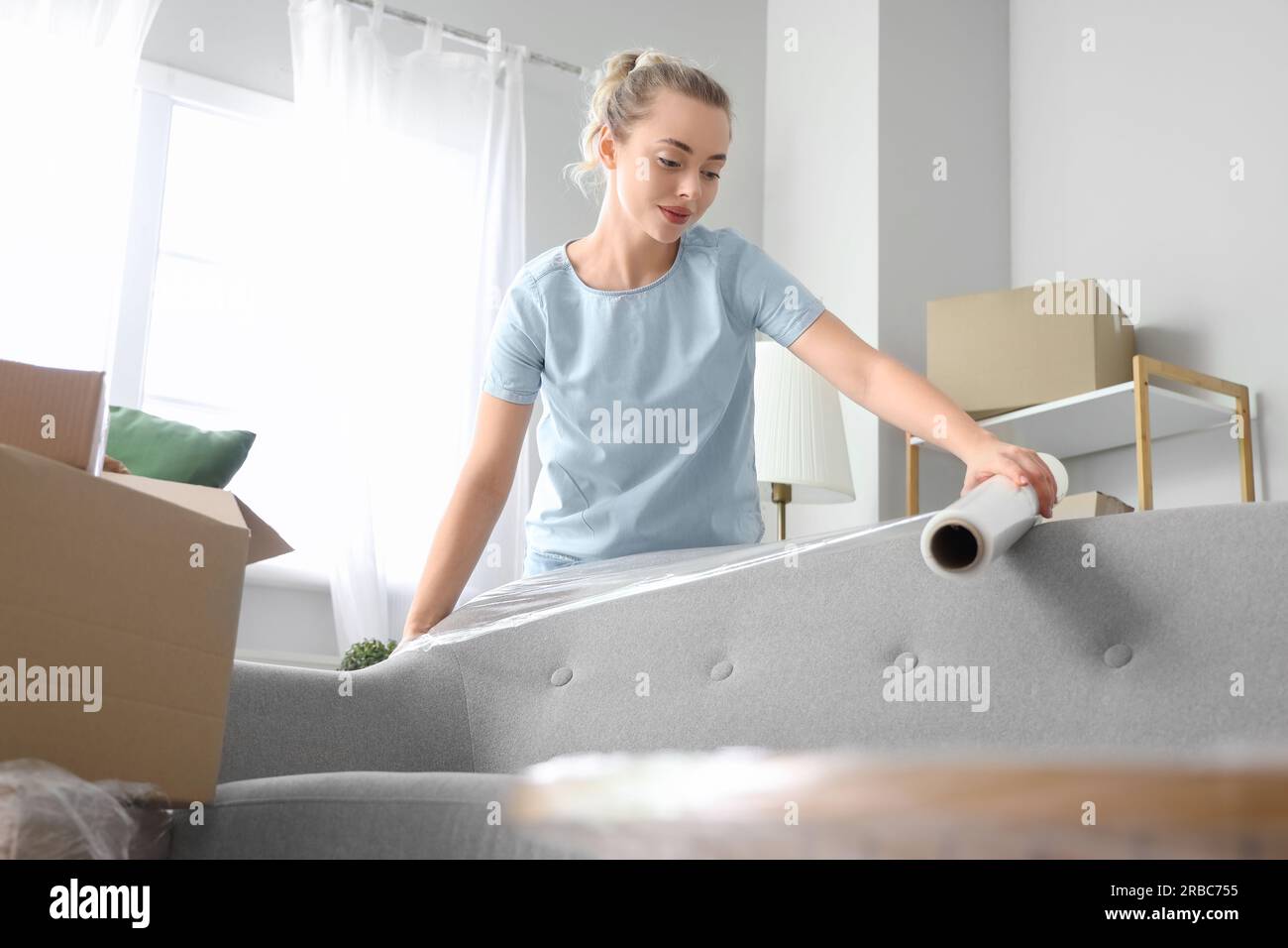 Young woman wrapping sofa with stretch film at home Stock Photo - Alamy
