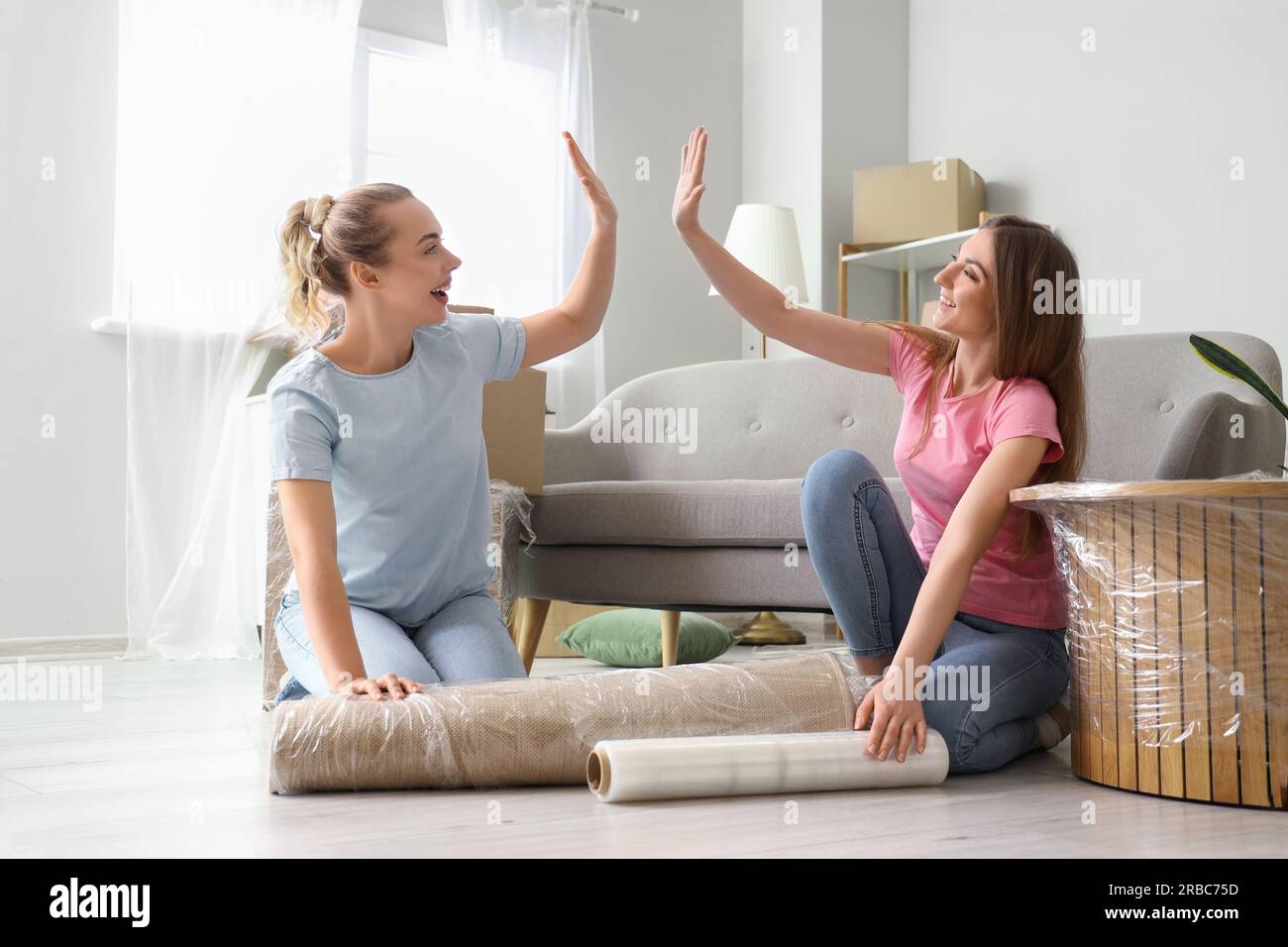 Young women wrapping carpet with stretch film at home Stock Photo - Alamy