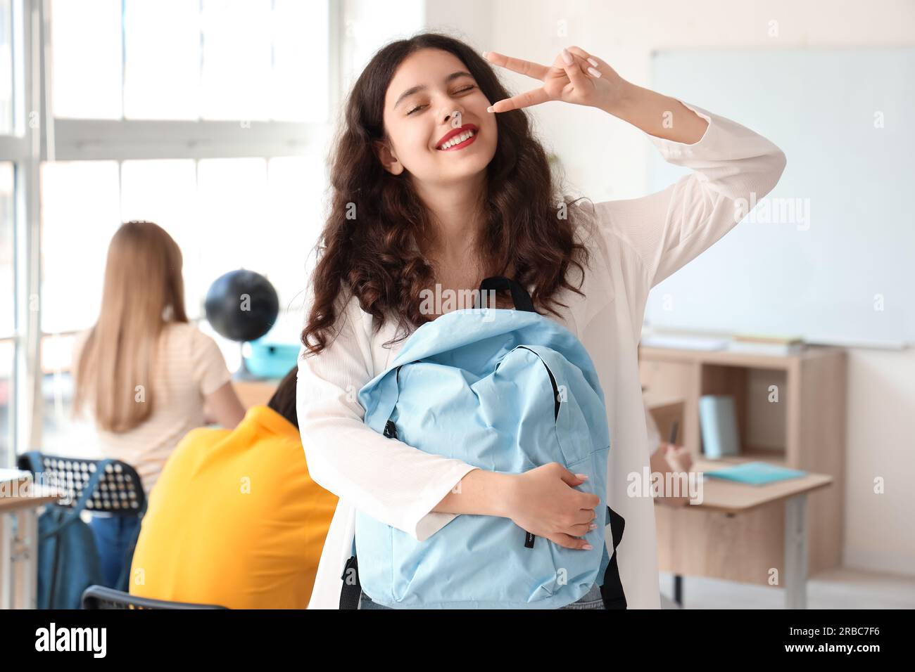 Female student with backpack showing victory gesture in classroom Stock ...