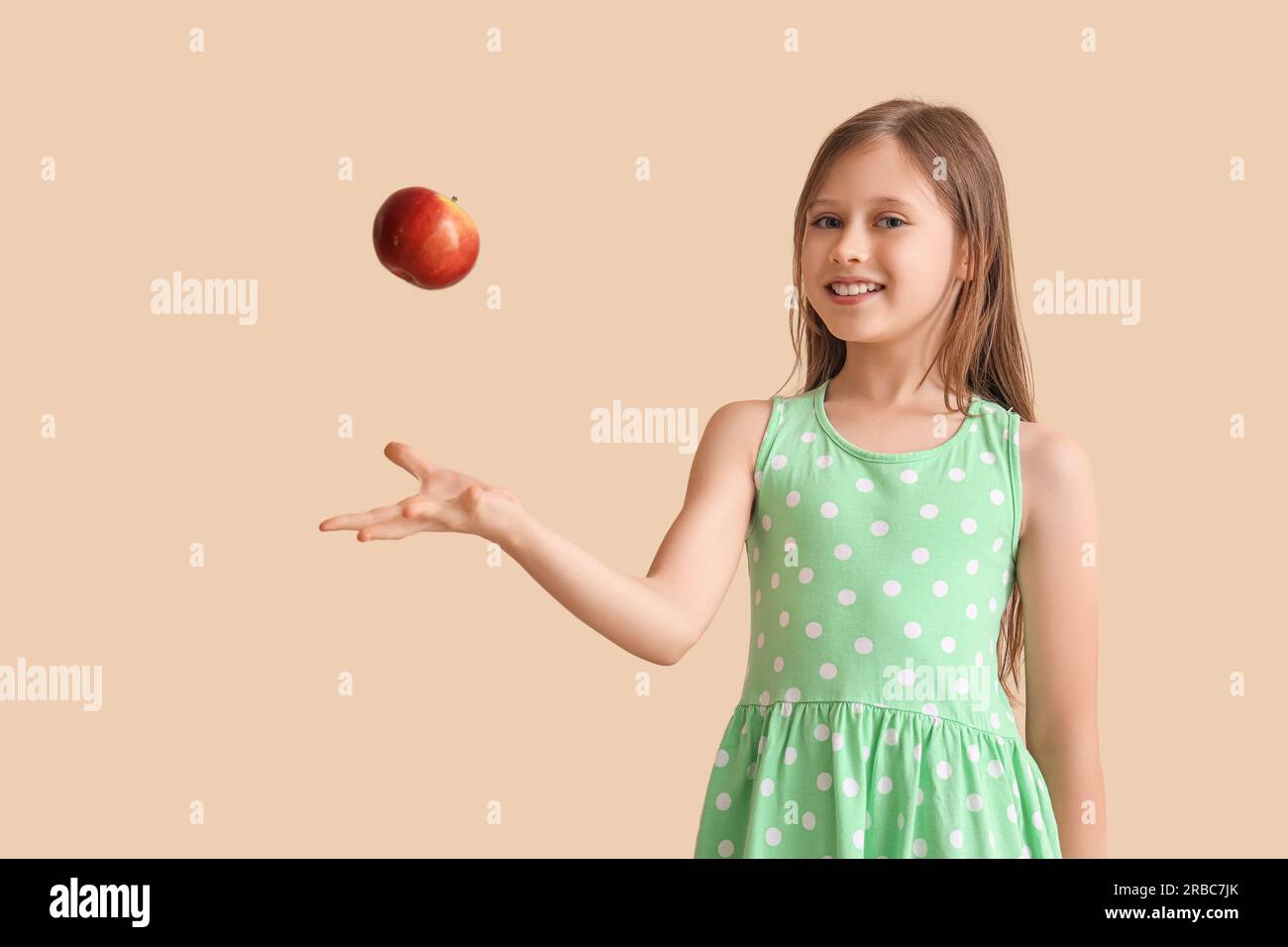 Little girl throwing apple on beige background Stock Photo - Alamy