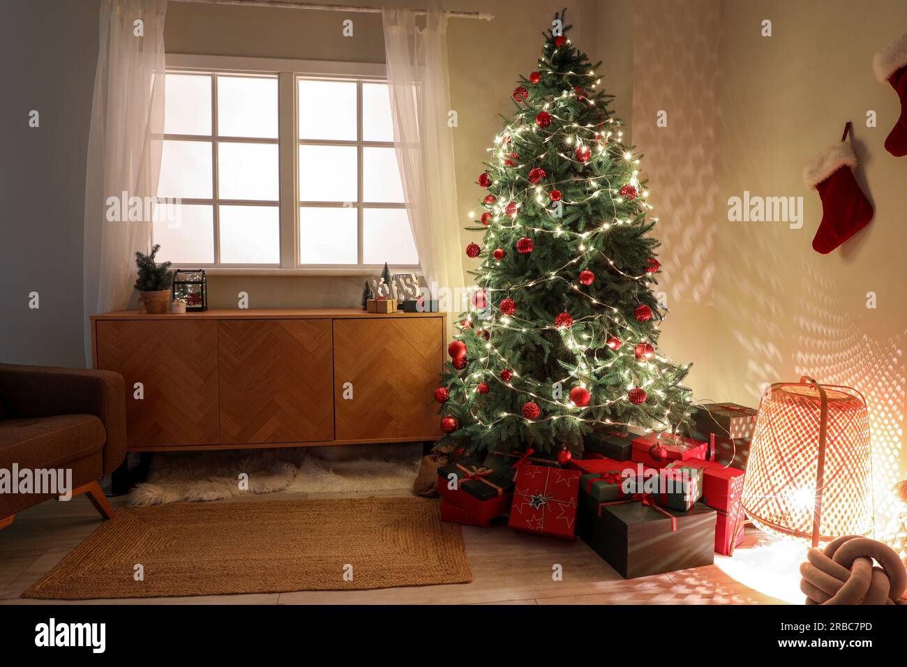 Christmas tree with glowing lights, gifts and wooden chest of drawers ...