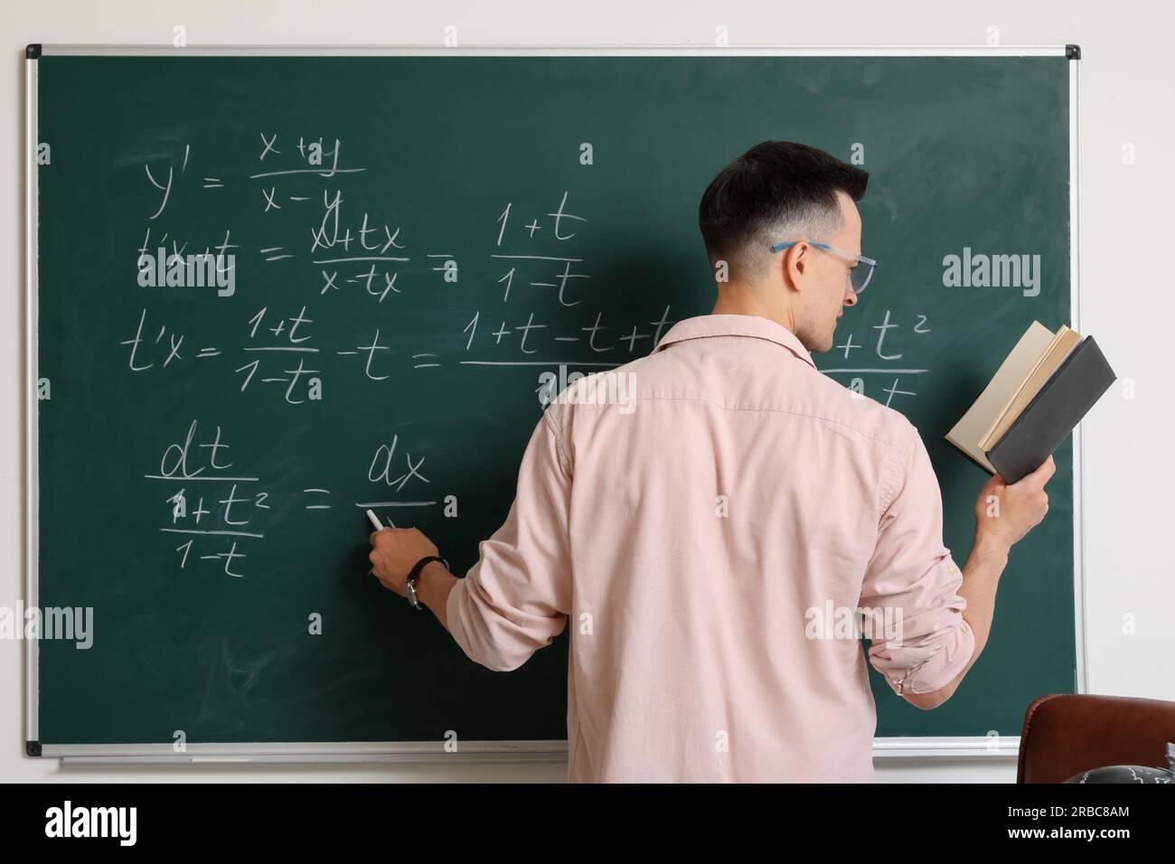 Male Math teacher conducting lesson near chalkboard in classroom, back ...
