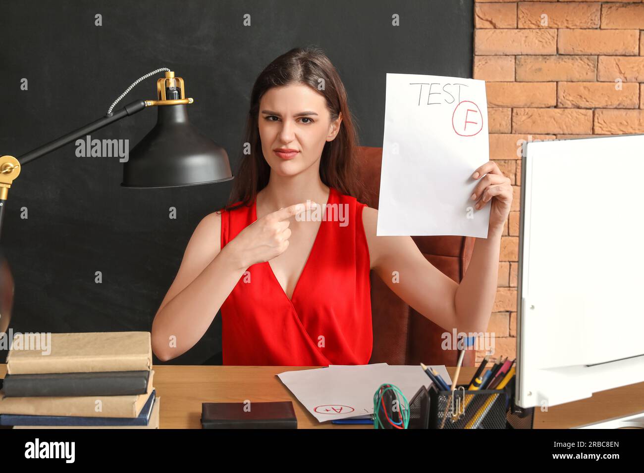 Female teacher pointing at checked test sheet at table in classroom ...