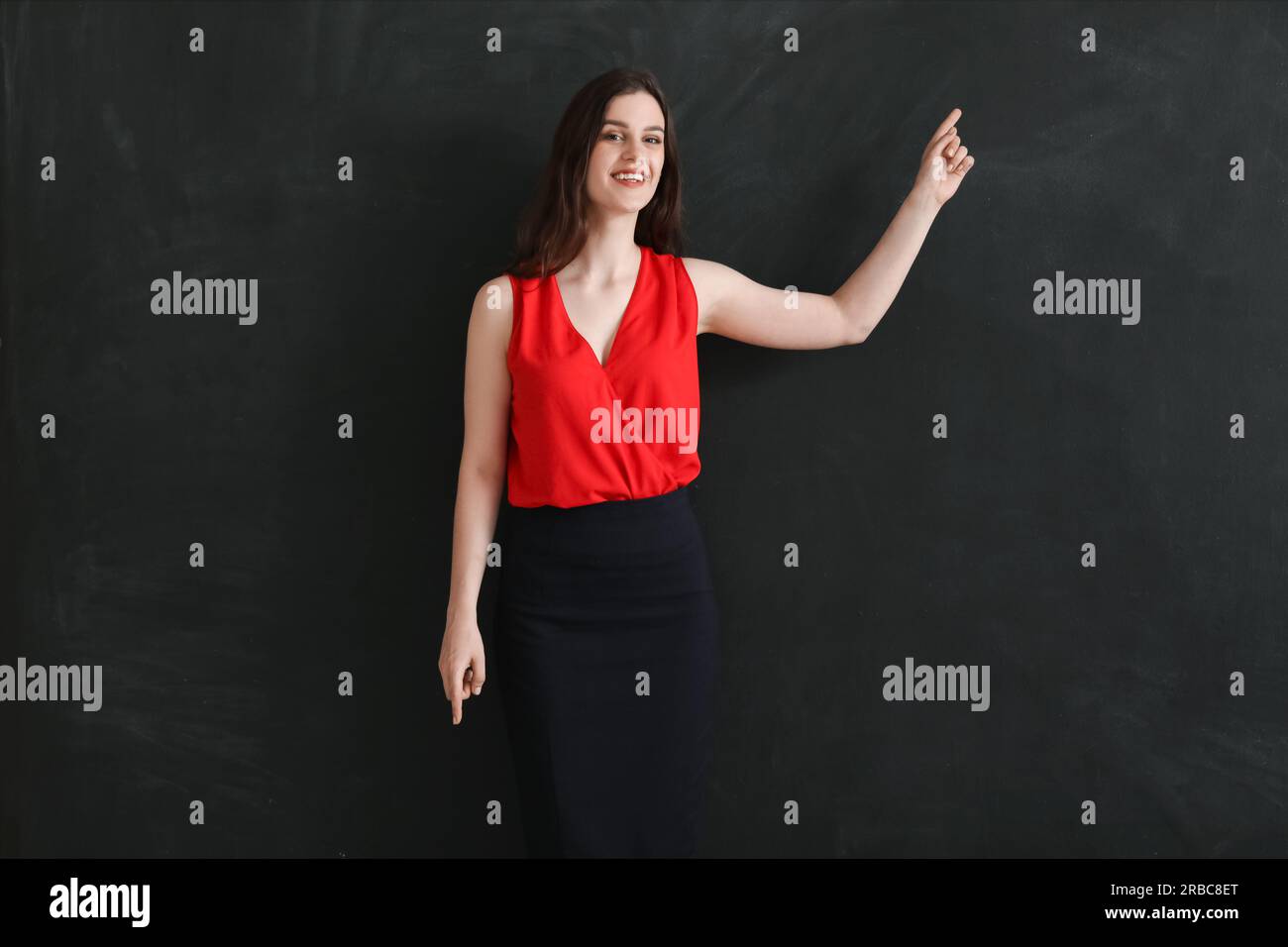 Female teacher pointing at something near blackboard in classroom Stock ...