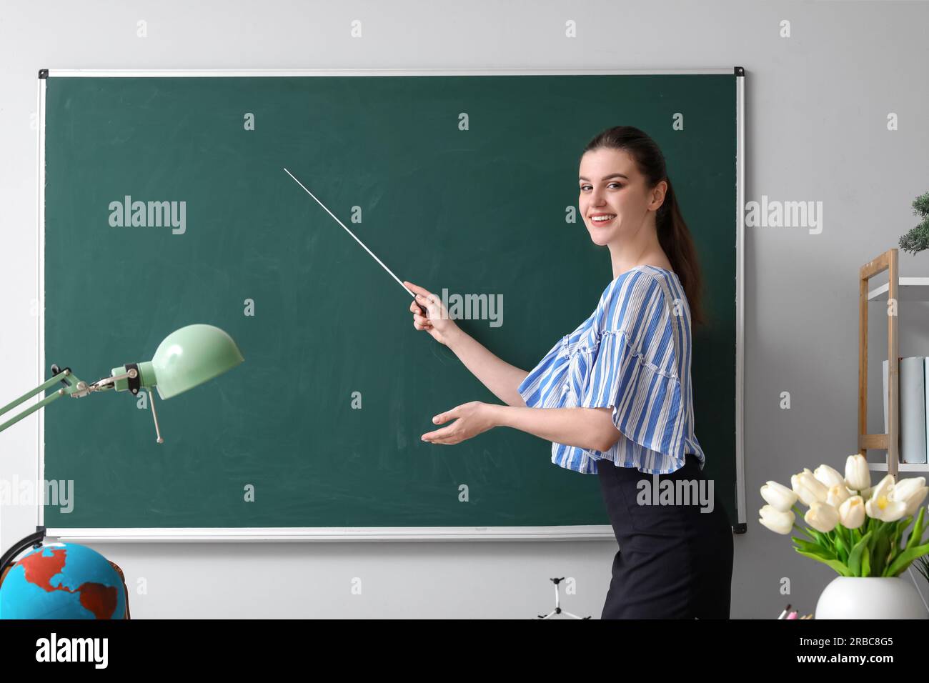 Female teacher with pointer near chalkboard in classroom Stock Photo ...
